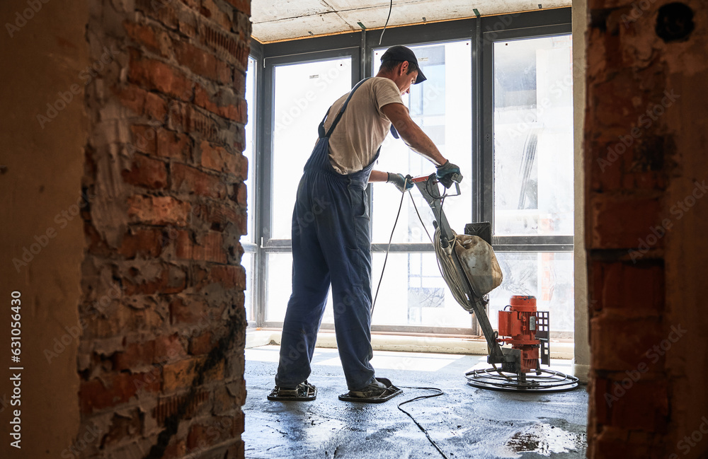 Full length of male worker using troweling machine while screeding ...