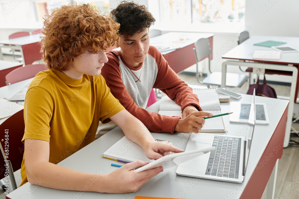 Teenage schoolboys using devices together during lesson in classroom at ...