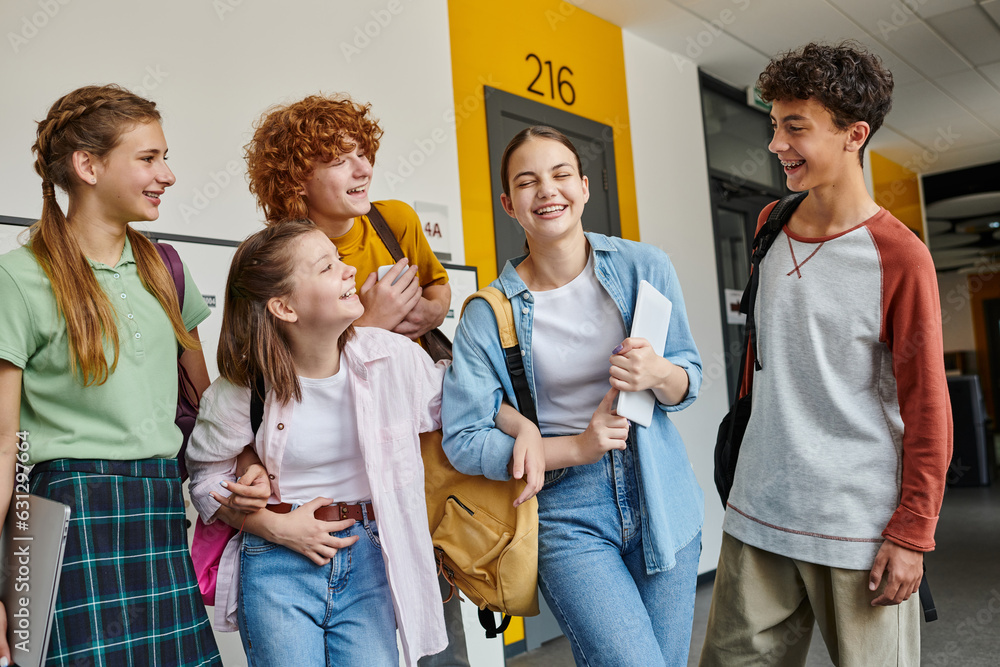 teenage schoolkids laughing and standing in school hallway together ...