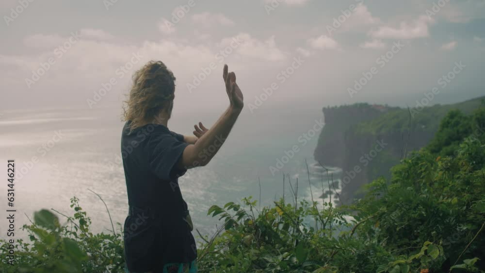 A man with long curly hair stay in on edge of ocean cliff moving hands ...