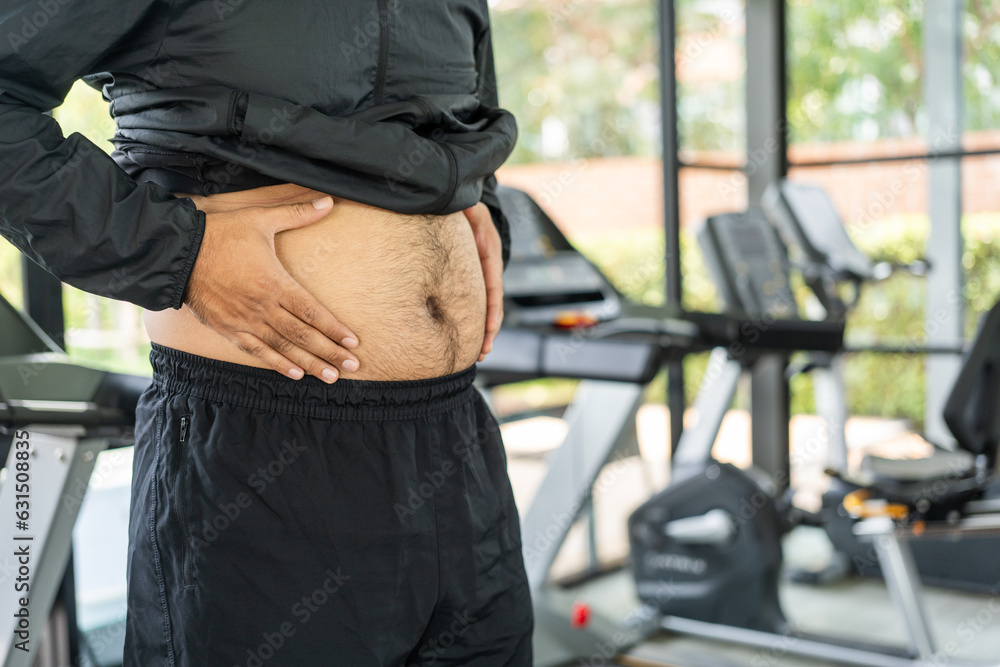 Young fitness Man touching his fat belly in sport gym background ...