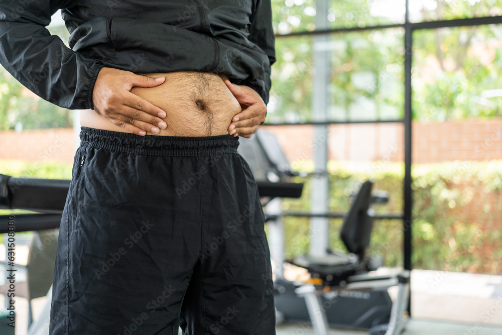 Young fitness Man touching his fat belly in sport gym background ...