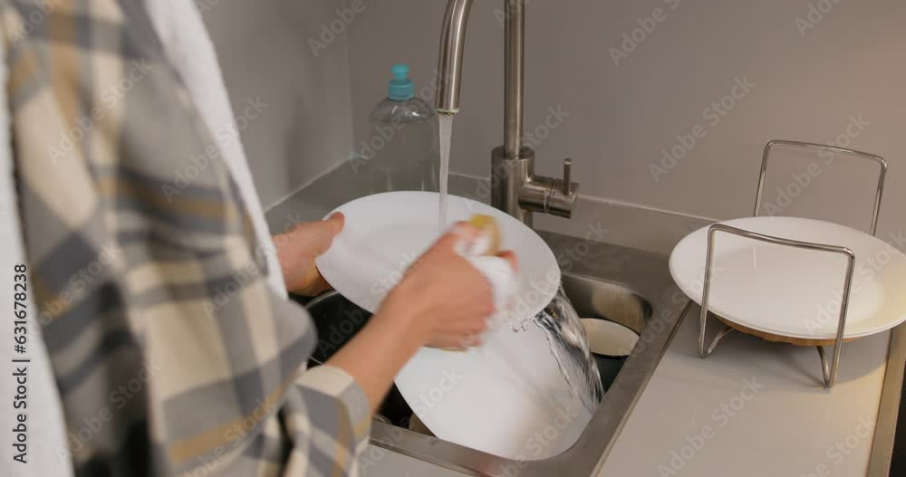 Woman housewife in casual clothes washing plates under running water in ...