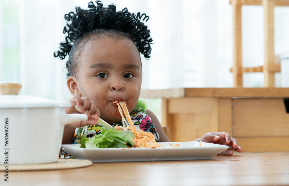 Portrait of little African hungry toddler girl eating spaghetti and ...