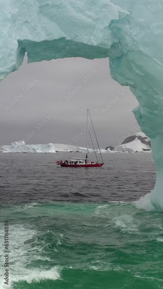Vertical video view of ship through arch of huge white iceberg in ...