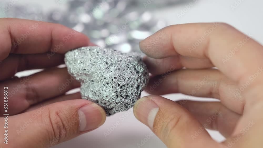 Man's hand holding a lump of silver or platinum or a rare earth mineral ...