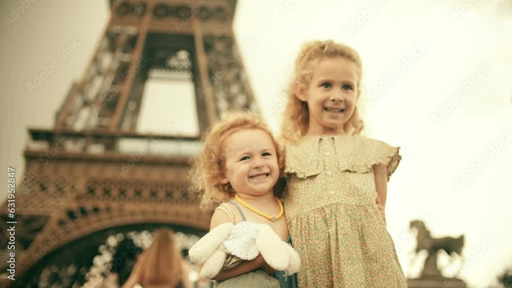 Two smiling little sisters hug each other and pose at the famous Eiffel ...