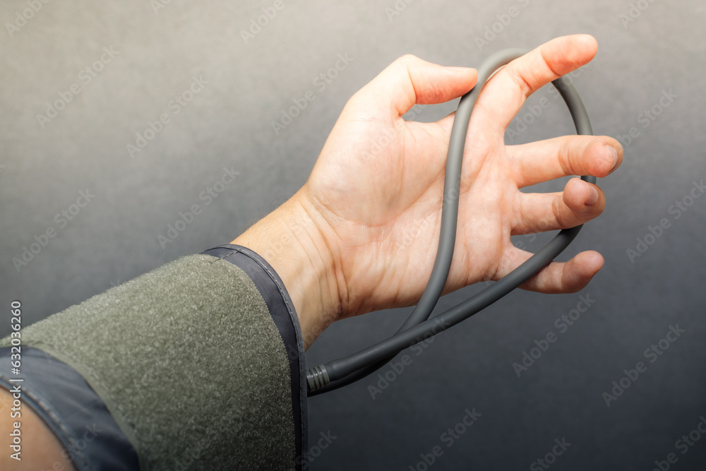 Man holds Blood Pressure Cuff in his hand and arm is in tension. Rays ...