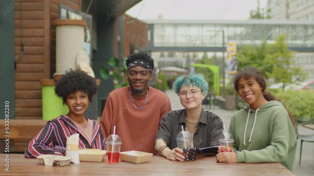 Group portrait of diverse gen Z friends sitting with food and drinks in ...