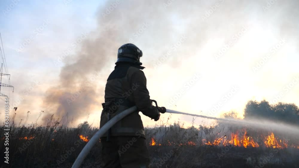 Male firefighter in uniform extinguishes burning dry grass using fire ...