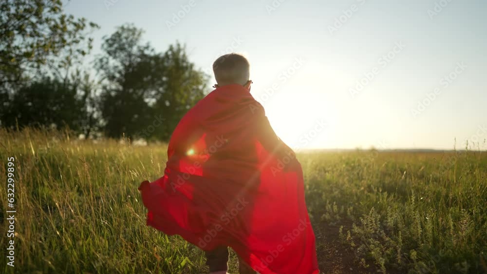 Happy child hero runs on green grass. Boy in a red superhero cape ...