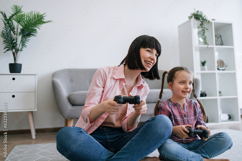 Portrait of cheerful mother and cute daughter sitting cross-legged with ...