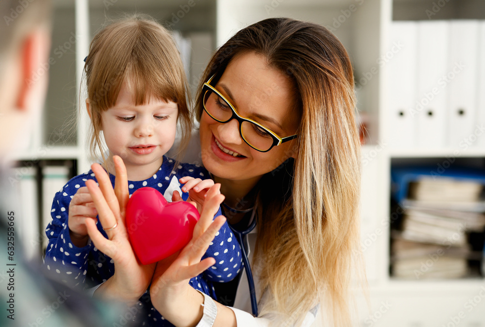 Female doctor and happy little child hold in arms red toy heart closeup ...