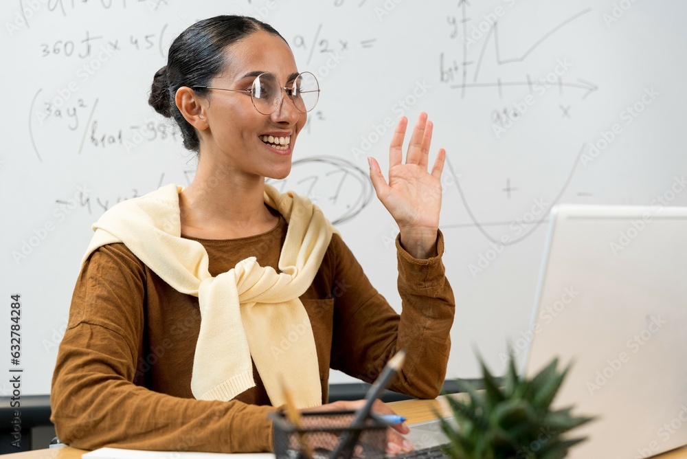 Educator saying hello to her students on laptop sitting in classroom ...