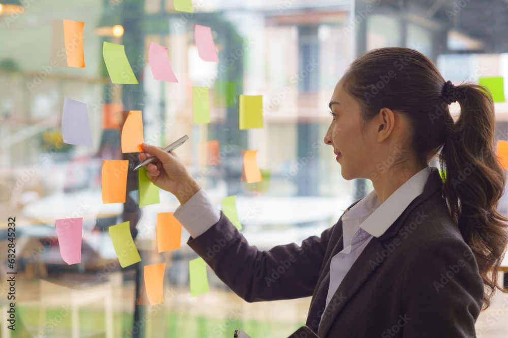 Asian businesswomen use post-it notes on glass walls to write strategic ...