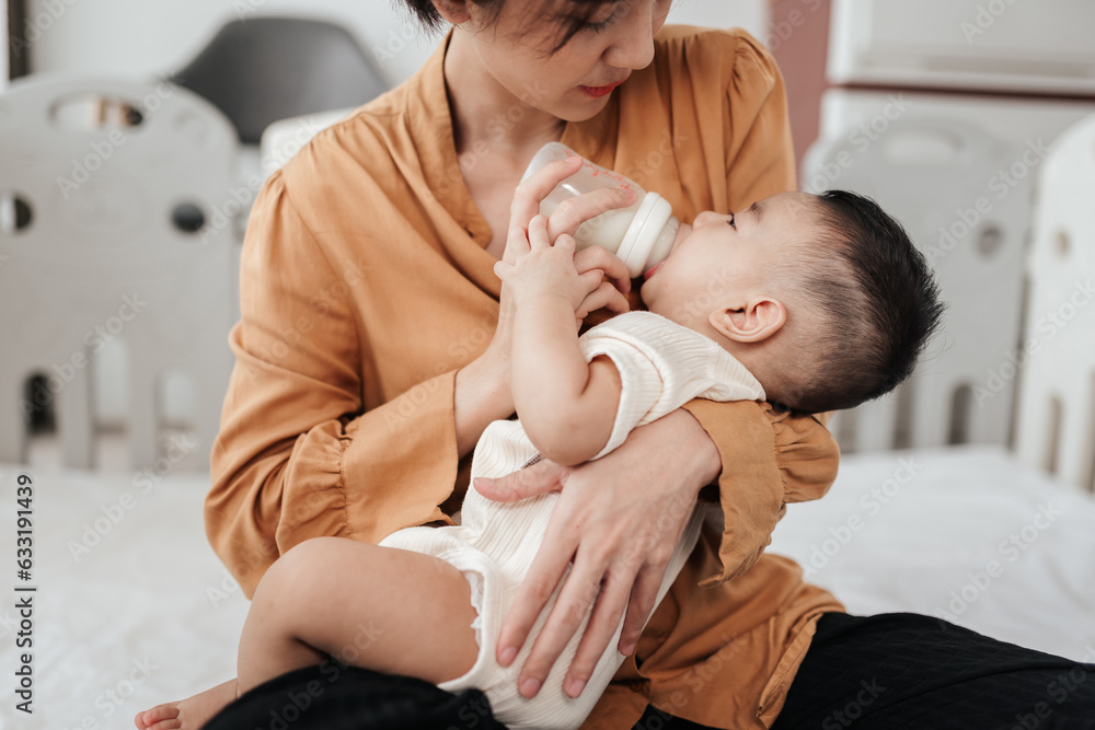 Adorable little Asian baby sleep during drinking milk from baby bottle. Asian mother holding ...