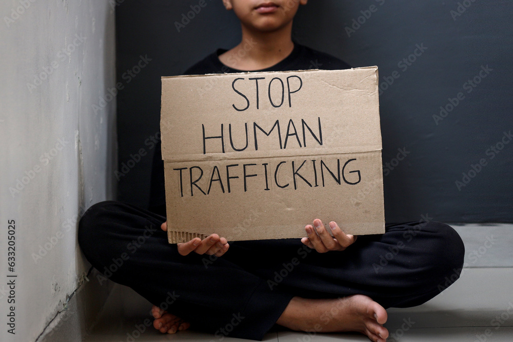 A little boy sitting crossed legs holding cardboard with text Stop ...