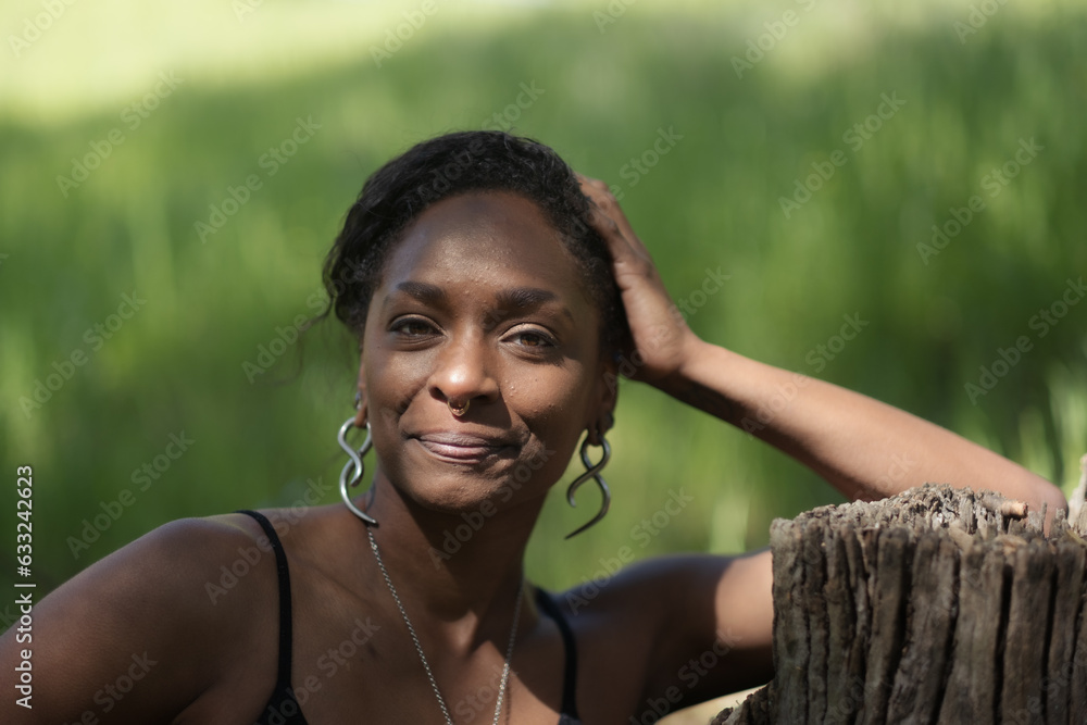 A person leans against a tree stump and smiles, leaning their head on ...
