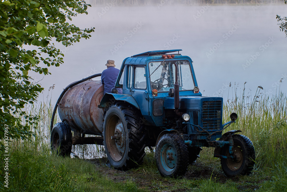 Blue wheeled agricultural tractor with tank trailer is refueled with ...