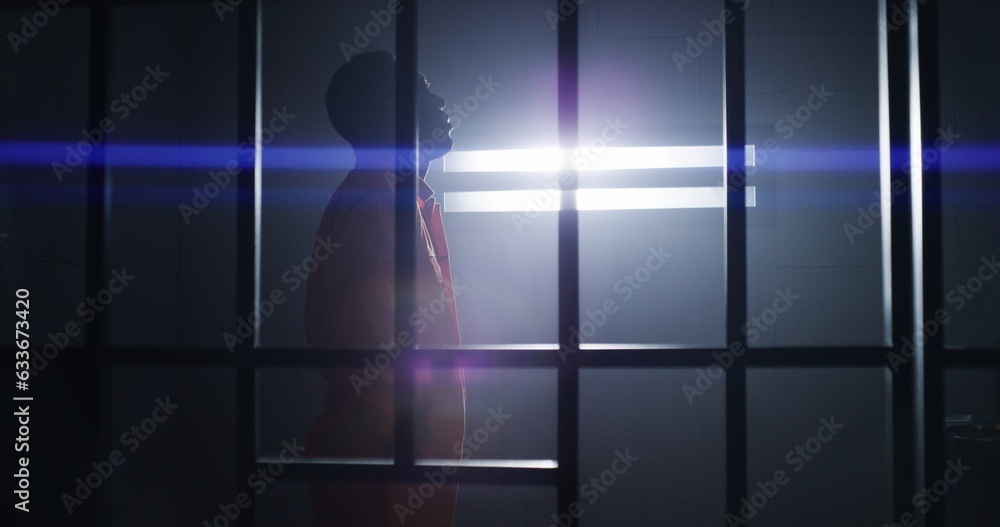 Depressed African American man in orange uniform stands from jail bed ...