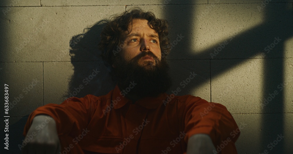 Depressed male prisoner in orange uniform sits in prison cell, lights ...