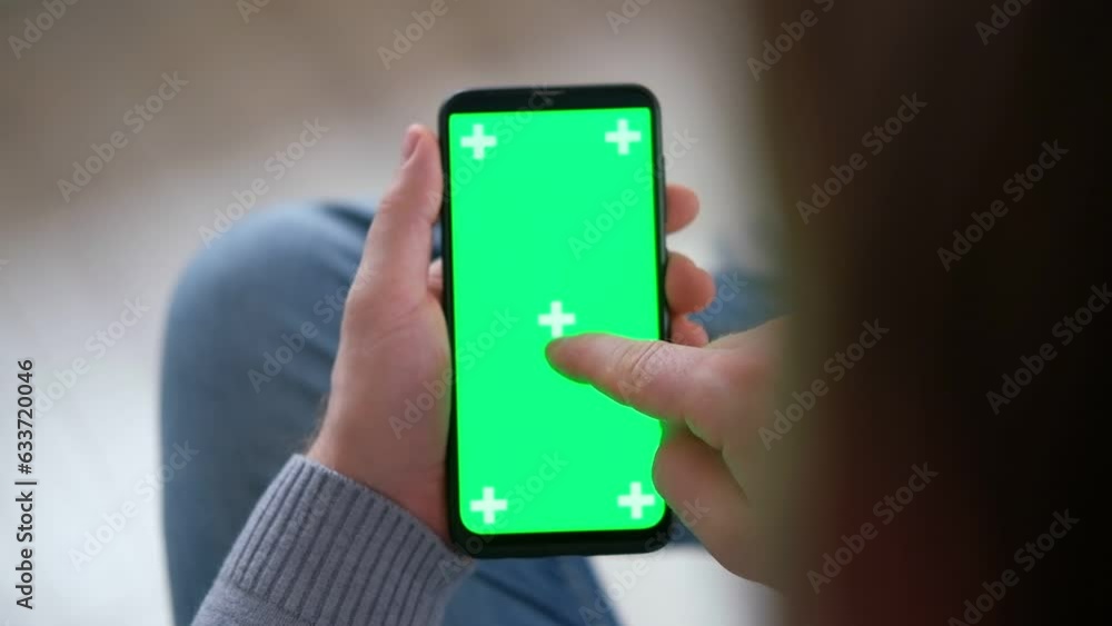 Young man sitting at home holding smartphone greenscreen mock-up in ...