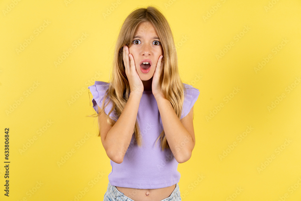 Scared terrified blonde kid girl wearing violet T-shirt over yellow ...