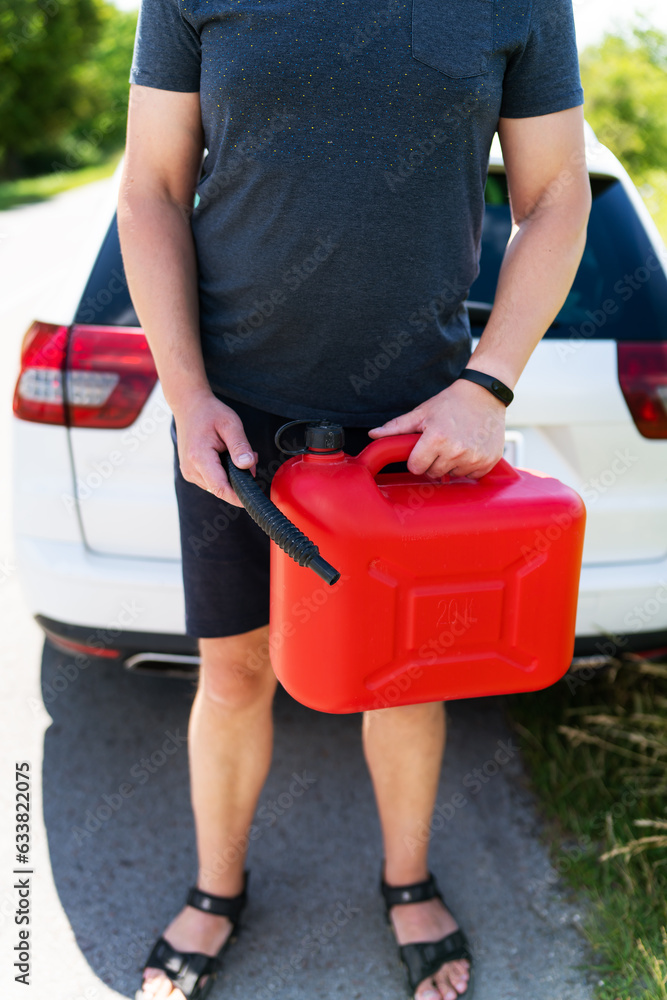 A man is holding a red can next to a white car. Stop to refuel ...