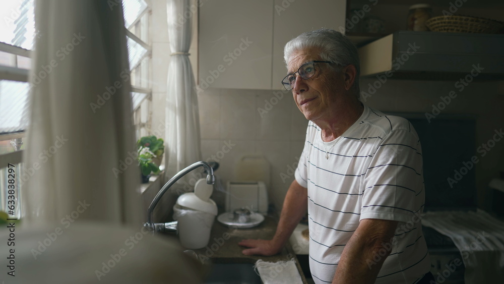 Thoughtful Senior Man Gazing Out of Kitchen Window, Leaning on Counter ...