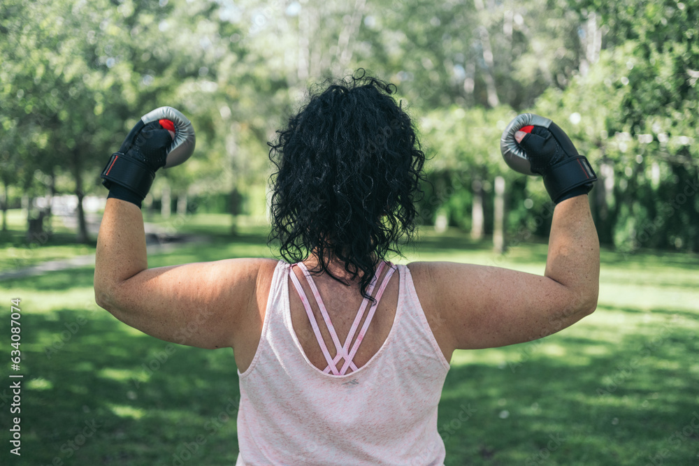 Female athlete with street boxing gloves on her back raising her arms ...
