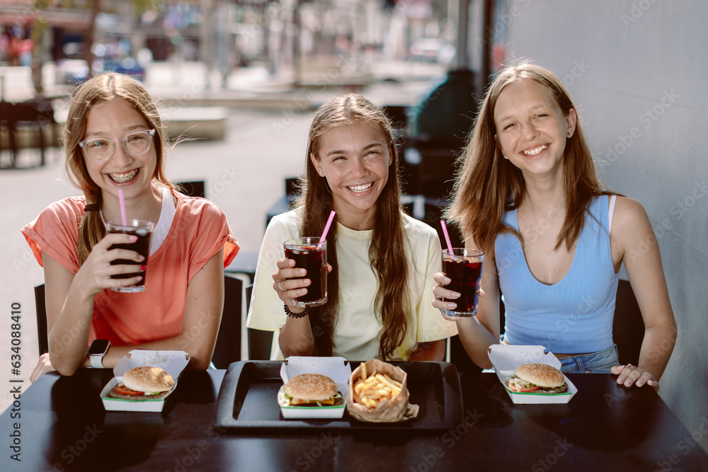 Three joyful smiling teenage girls (14-15 years old) sitting at a cafe ...