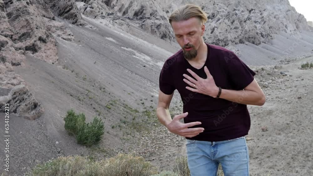 A slender stylish young man with long hair meditates in the mountains ...