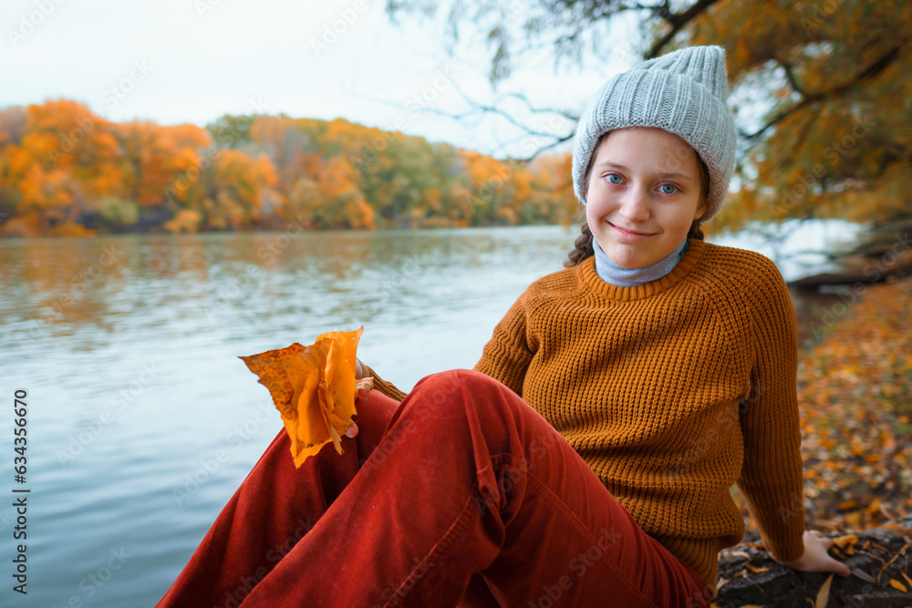 a young teenage girl posing in an autumn forest, sitting on a tree by ...