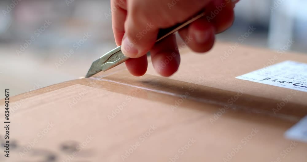 Close up hand hold Cutter Knife cut tape attached on the delivery box ...