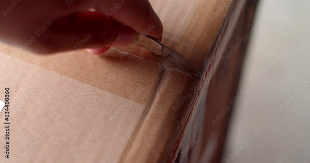 Close up hand hold Cutter Knife cut tape attached on the delivery box ...