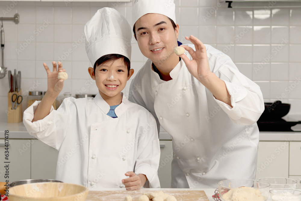 Happy Asian son and father in chef uniform with hat showing bread dough ...