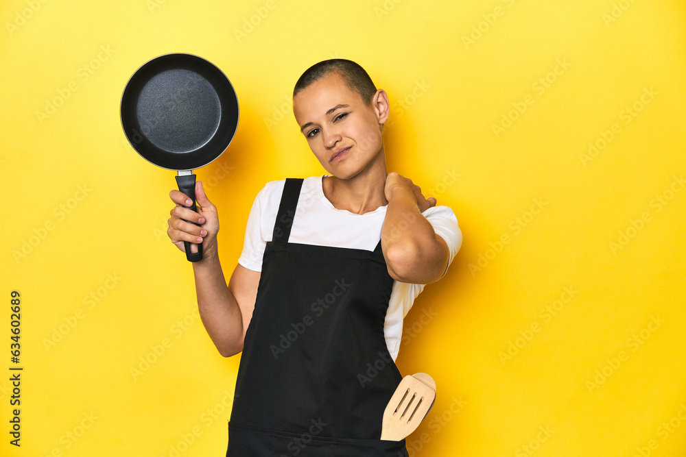 Cook woman holding a pan, yellow studio background touching back of ...