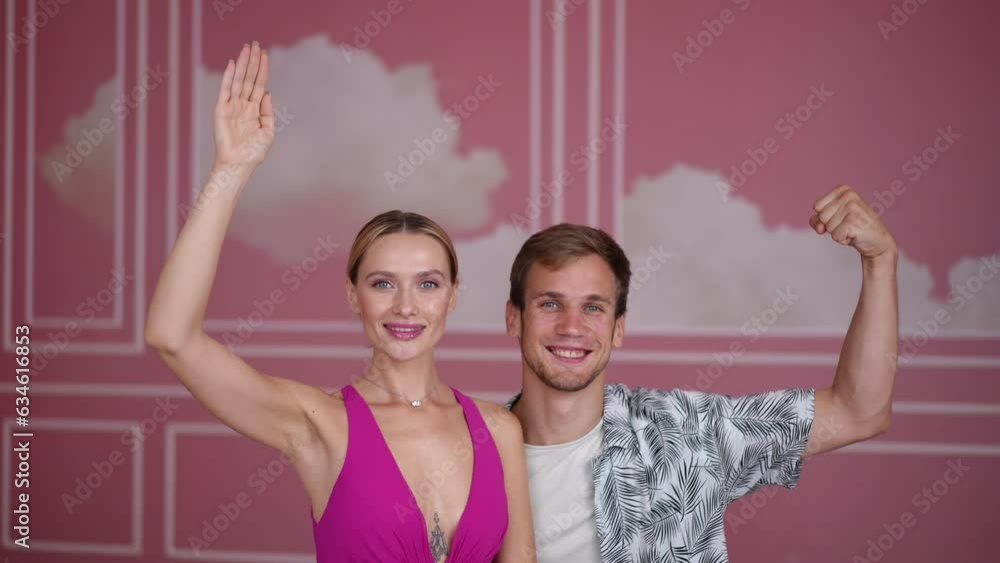 Beautiful woman waving looking at camera as man gesturing strength ...