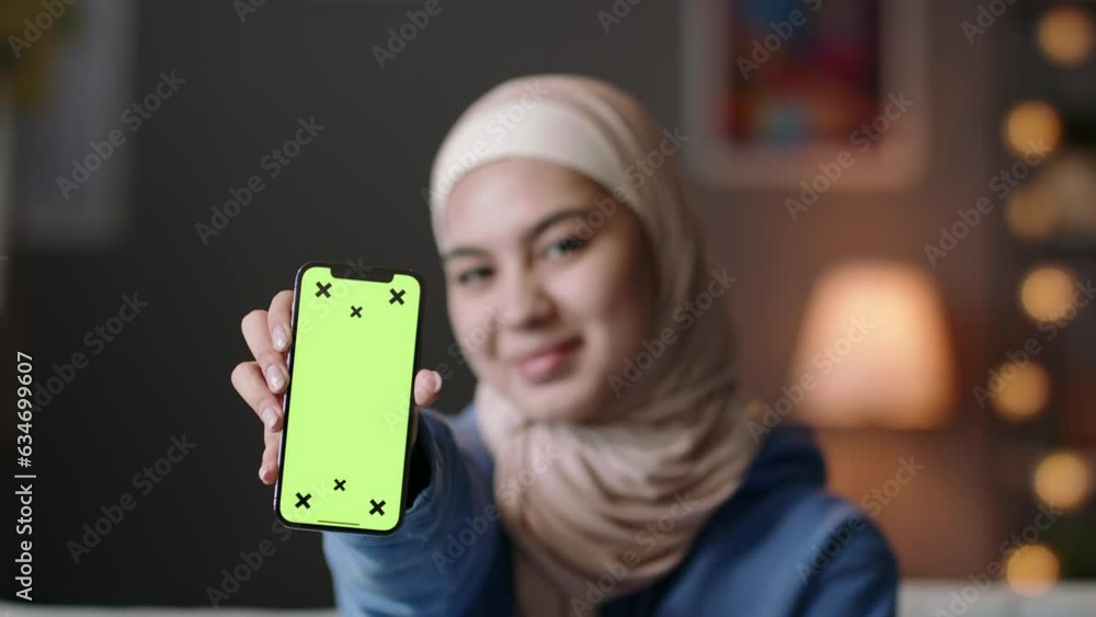 Smiling covered Muslim woman in hijab showing smartphone screen with ...