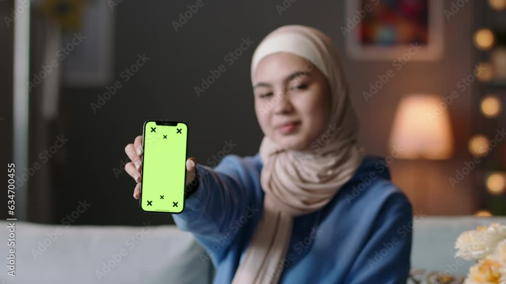 Smiling covered Muslim woman in hijab showing smartphone screen with ...