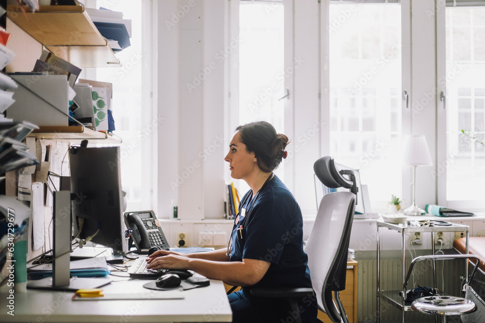 Side view of focused female healthcare worker using computer while ...