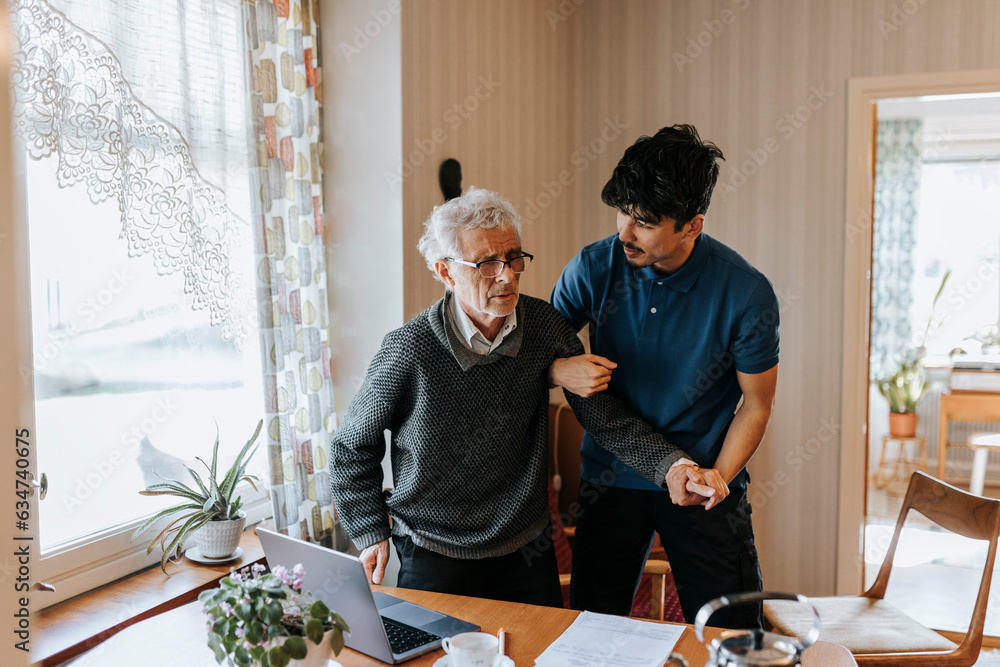 Male caregiver helping senior man while standing up at home Stock Photo ...