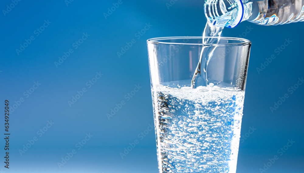 pouring water into a water glass, isolated drinking glass in front of a bright blue sunny and ...