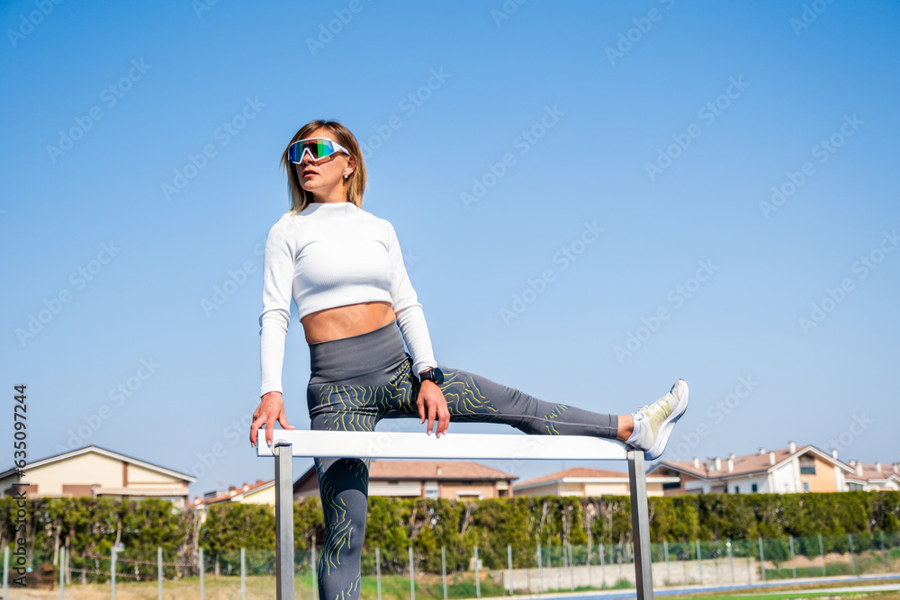 Athlete doing stretching exercises on the obstacle of running track ...