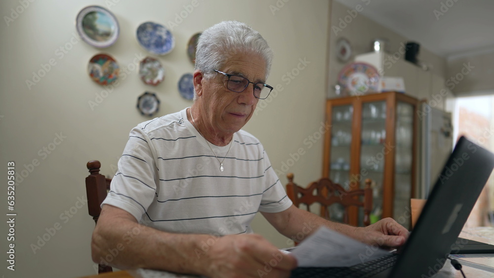 Worried senior man looking at fine paper in front of laptop computer ...