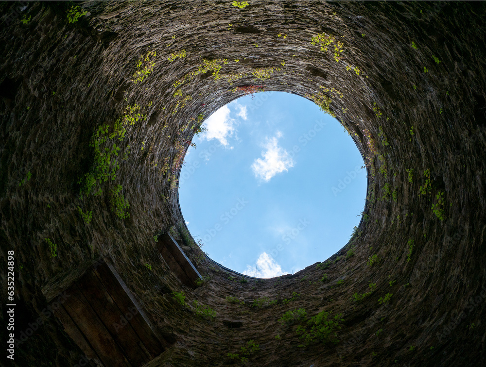 Stone well hole, old construction from inside, brick walls and blue sky ...