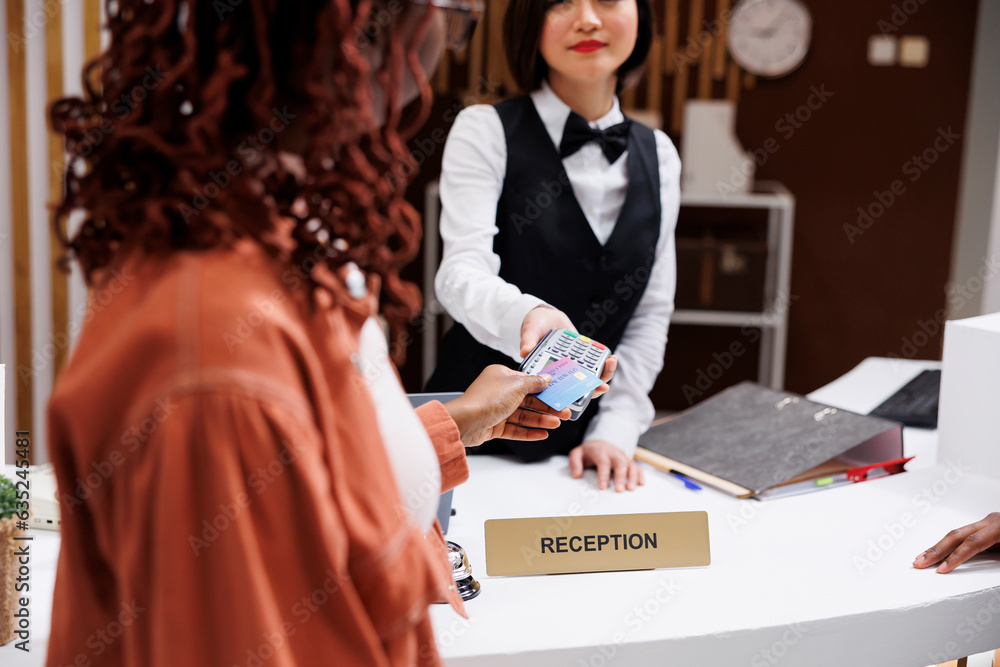 Young hotel guest paying for reservation at reception counter, using ...