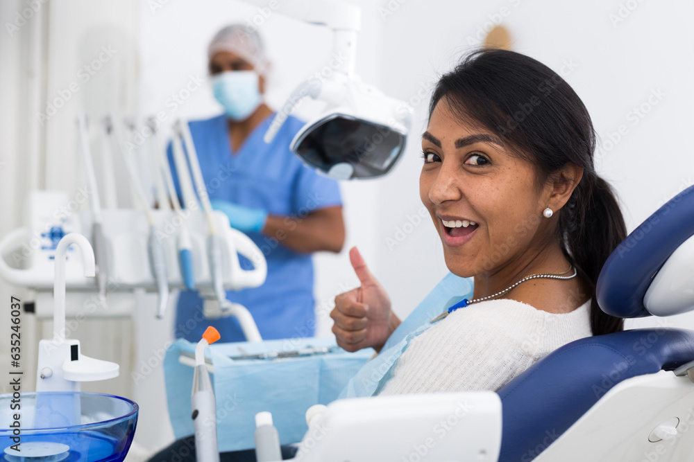 Smiling hispanic female patient showing thumb up after procedures in ...