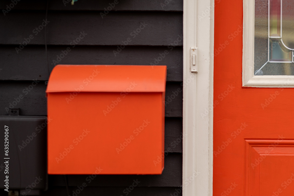 A square vibrant red metal mailbox on a navy blue wooden house with a ...