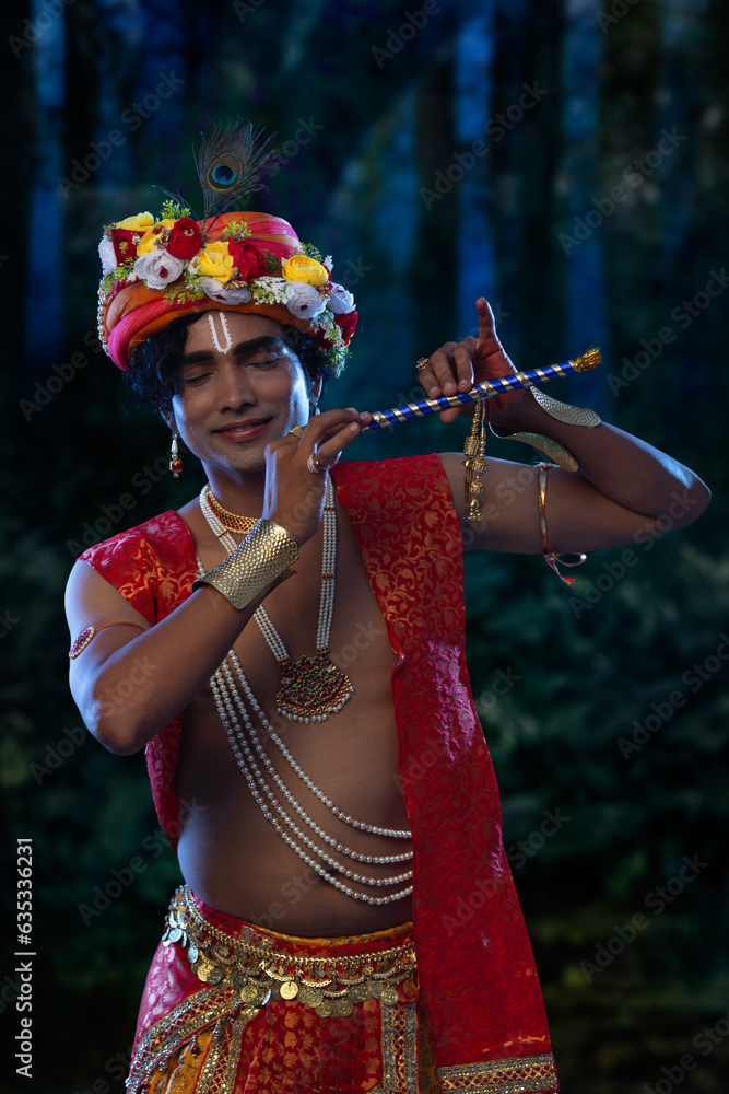 Portrait of young man dressed up as Lord Krishna and playing flute on ...